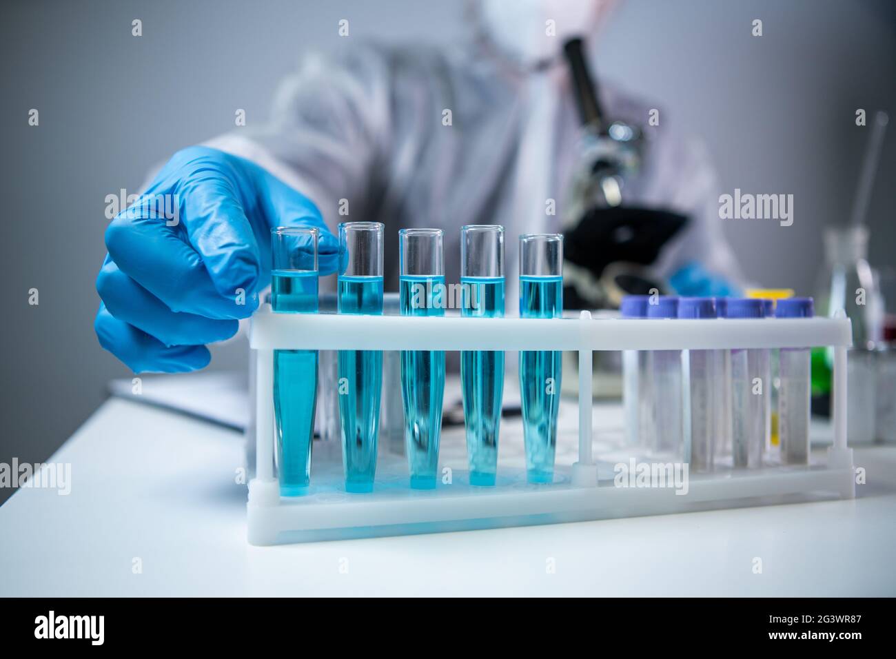 Scientist or medic in protective overalls, takes test tube with blue ...