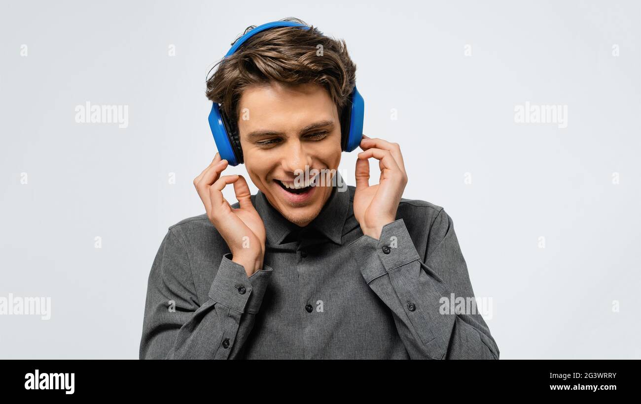 Joyful guy in grey shirt listening music wearing blue wireless ...