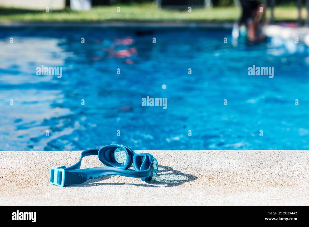 Blue swimming goggles on stone curb of swimming pool with blue water in ...