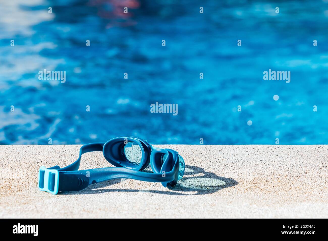 Blue swimming goggles on stone curb of swimming pool with blue water in ...