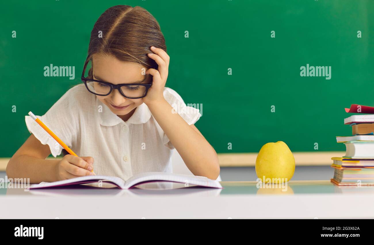 Concentrated schoolgirl child writing in copy-book while sitting at ...