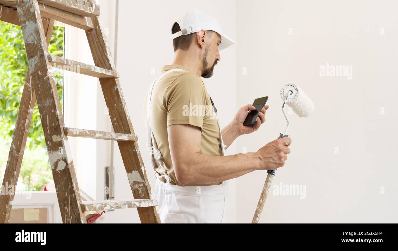 house painter man with mobile phone and paint roller, works the white ...