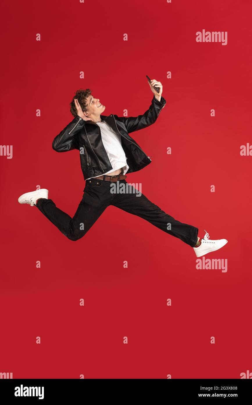 Always on mobile. Full length of young man taking phone while jumping ...