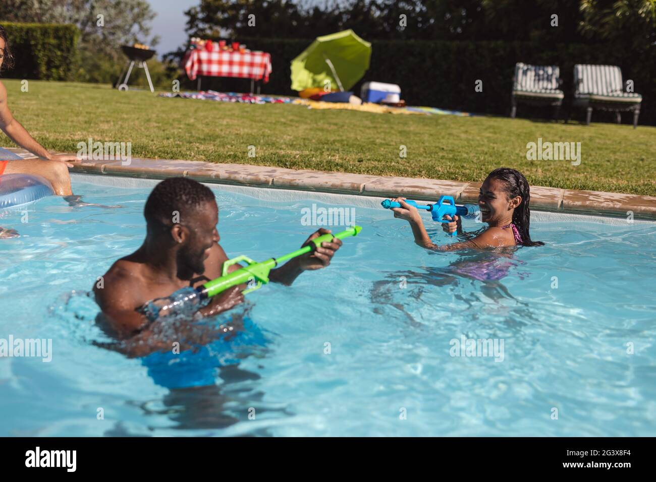Two diverse male and female friends having fun playing with water guns ...