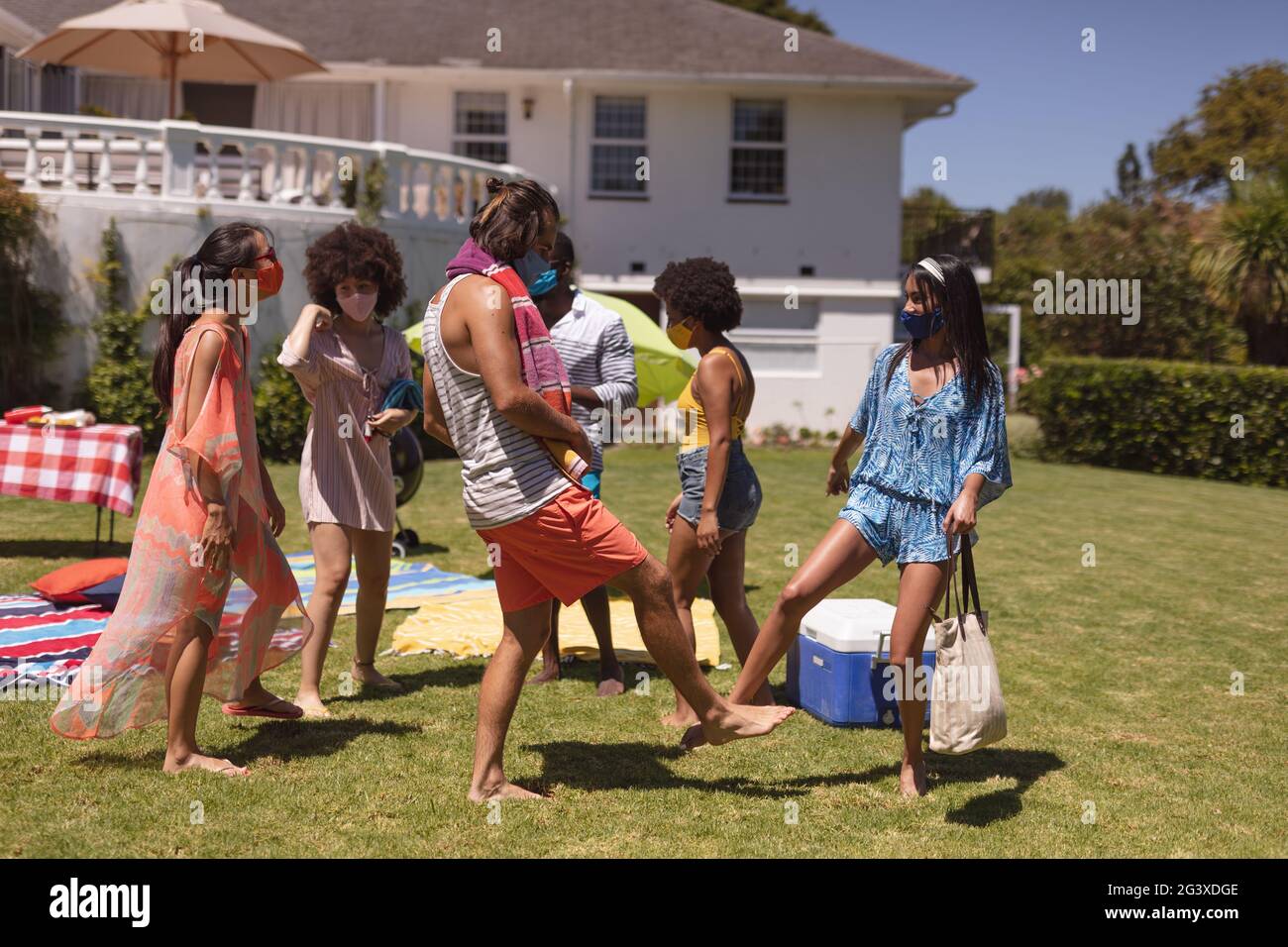 Group of diverse friends wearing face masks bumping legs at a pool ...