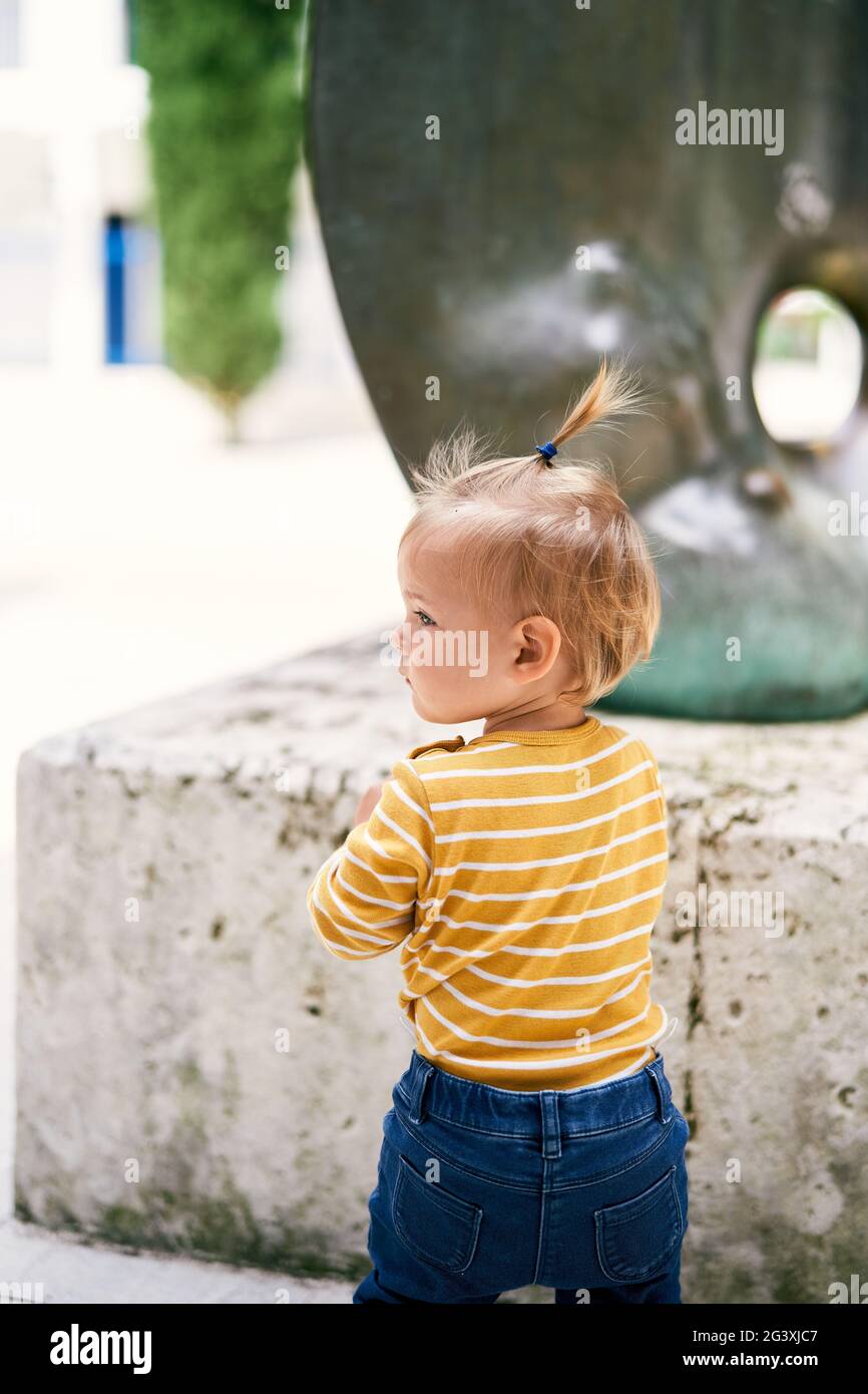 Little girl stands in front of the sculpture with her head turned to ...