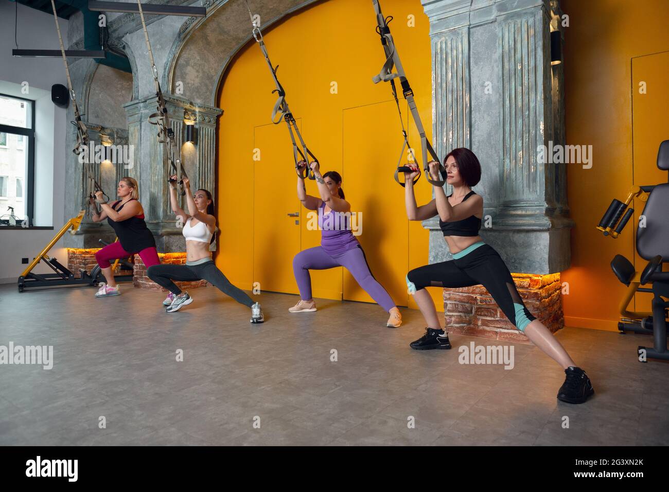 Athletic multinational people doing exercise with elastic rope in gym ...