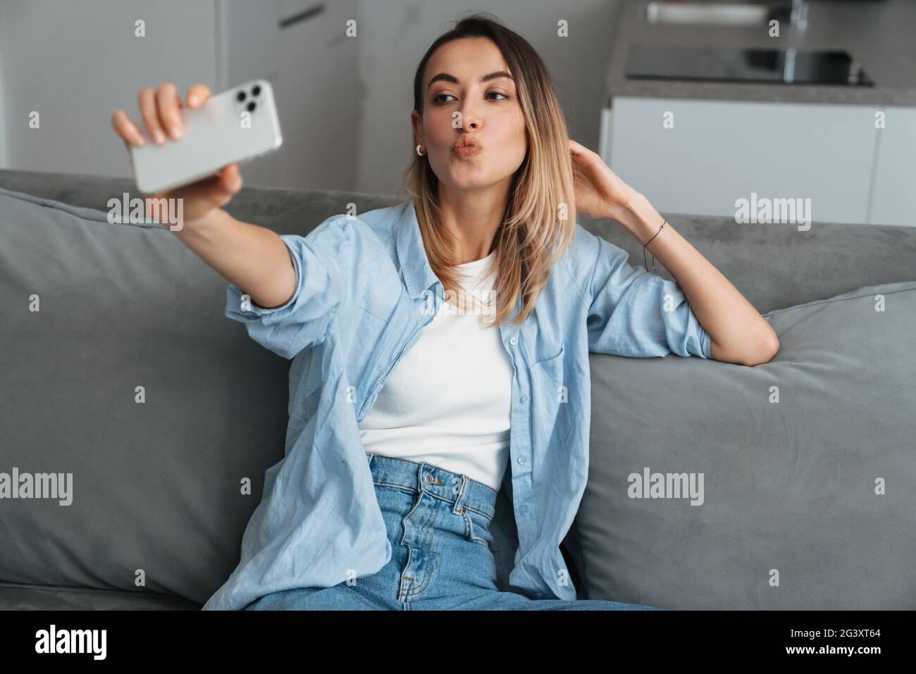 Lovely young woman taking a selfie while sitting on a couch at home ...