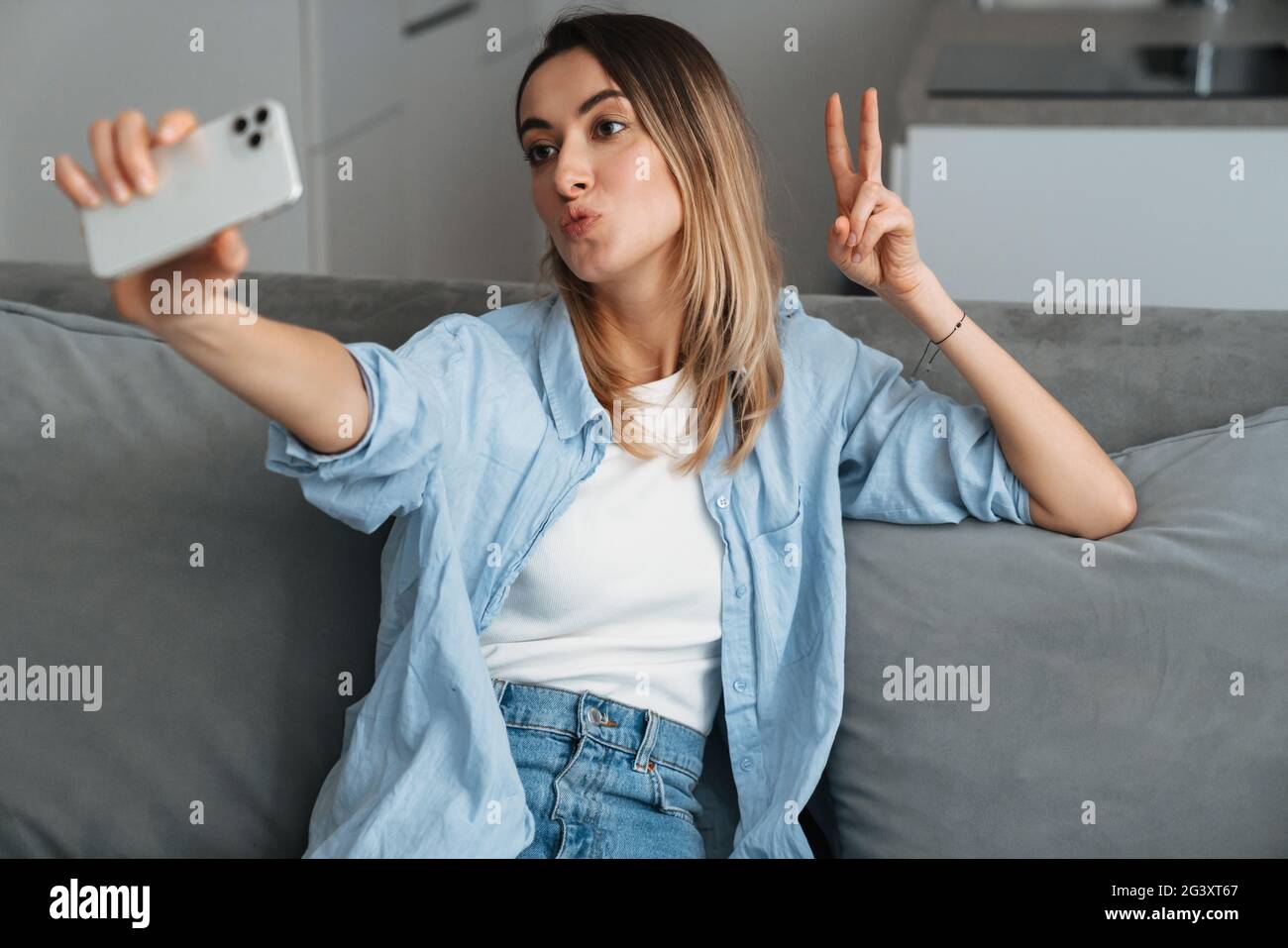 Lovely young woman taking a selfie while sitting on a couch at home ...