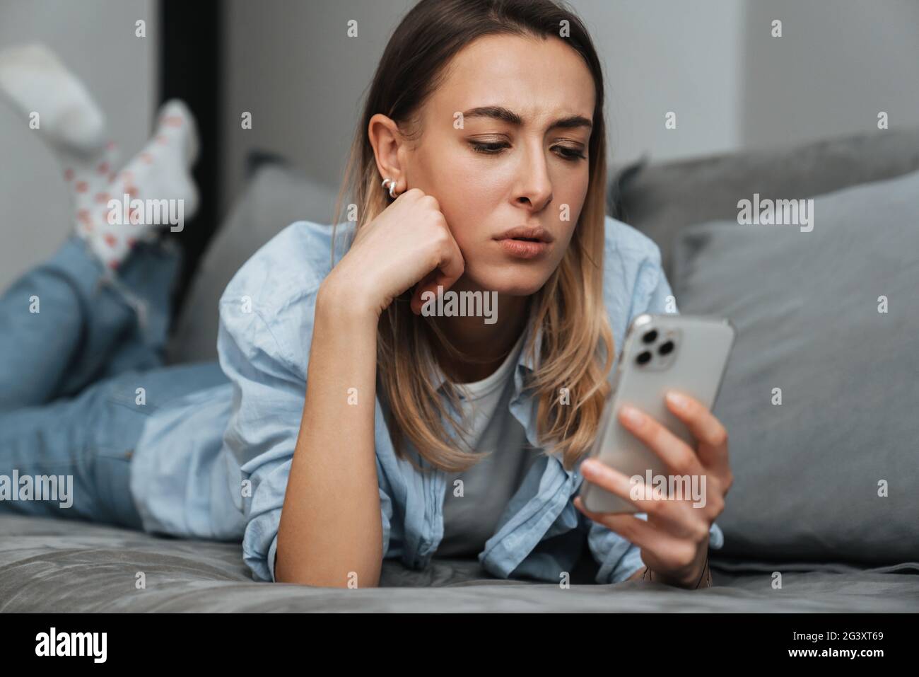 Confused Young Woman Looking At Mobile Phone While Laying On A Couch At