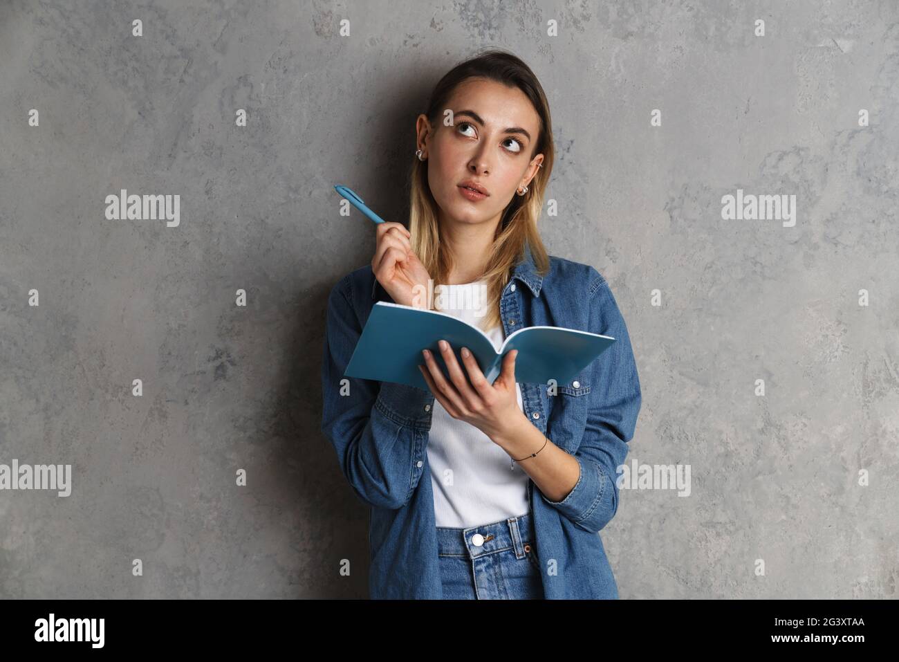 Pensive attractive young casual woman taking notes while standing ...