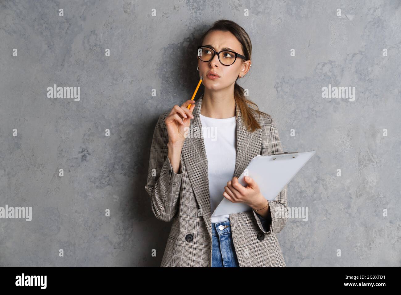 Pensive attractive young casual woman taking notes while standing ...