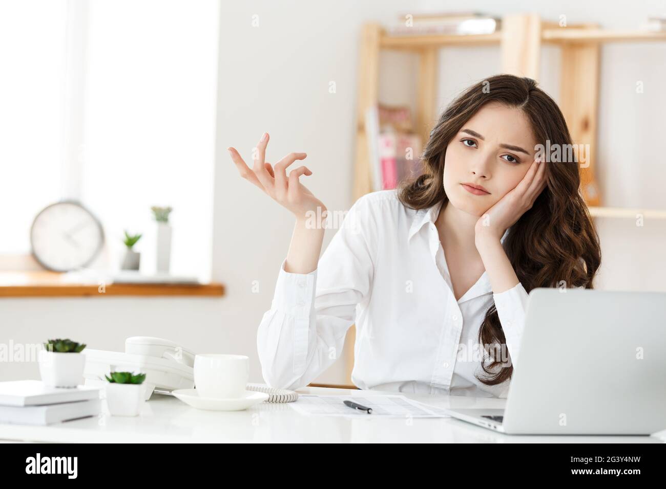 Thoughtful woman with hand under chin bored at work, looking away ...
