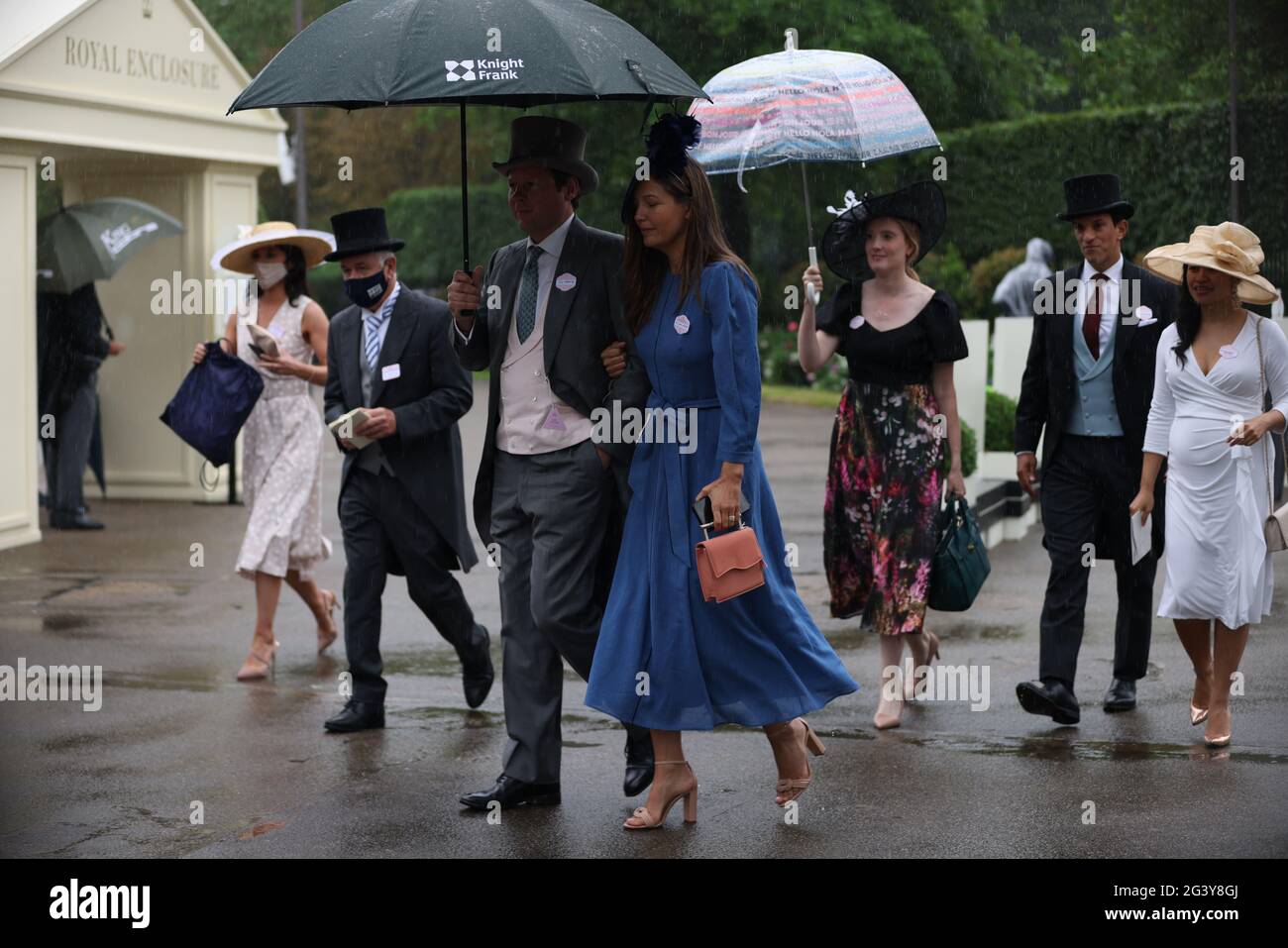 Racegoers take cover from the heavy rain under an umbrella during day ...