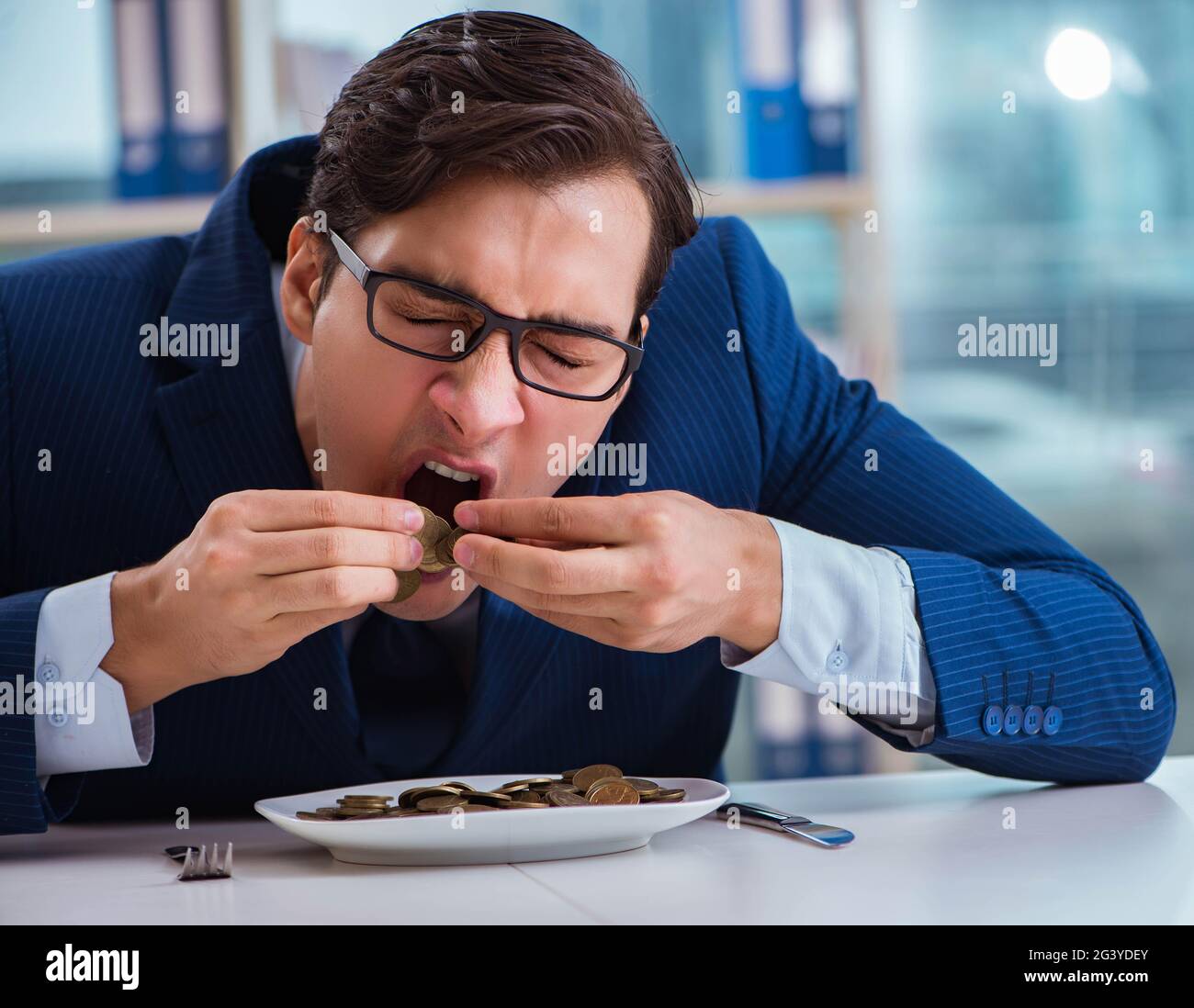 Funny businessman eating gold coins in office Stock Photo - Alamy