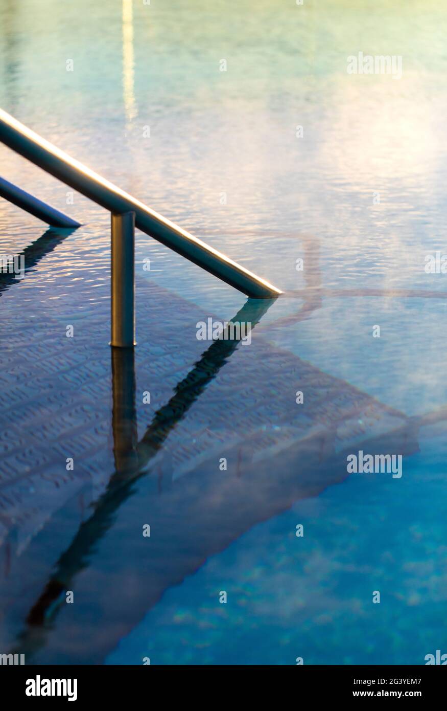 Detail shot of railing going into water in exterior pool, with morning ...