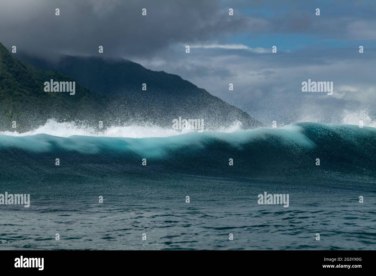 Breaking wave in the Teahupoo surfing area in front of a mountain ...