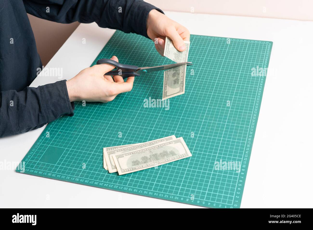 person's hand cutting a us hundred dollar cash banknote as a symbol of ...