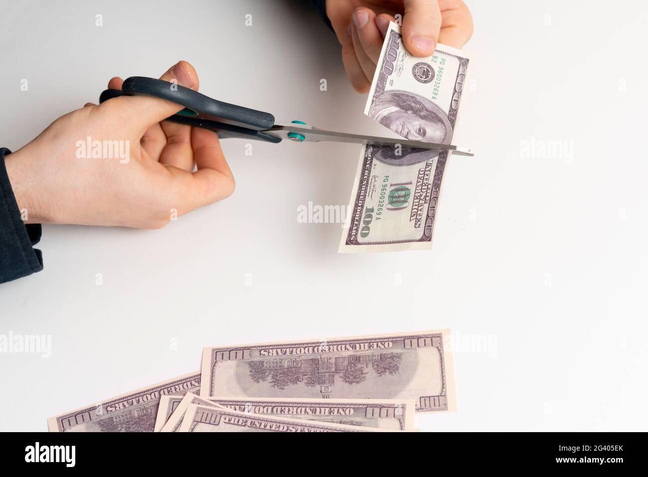 person's hand cutting a us hundred dollar cash banknote as a symbol of ...