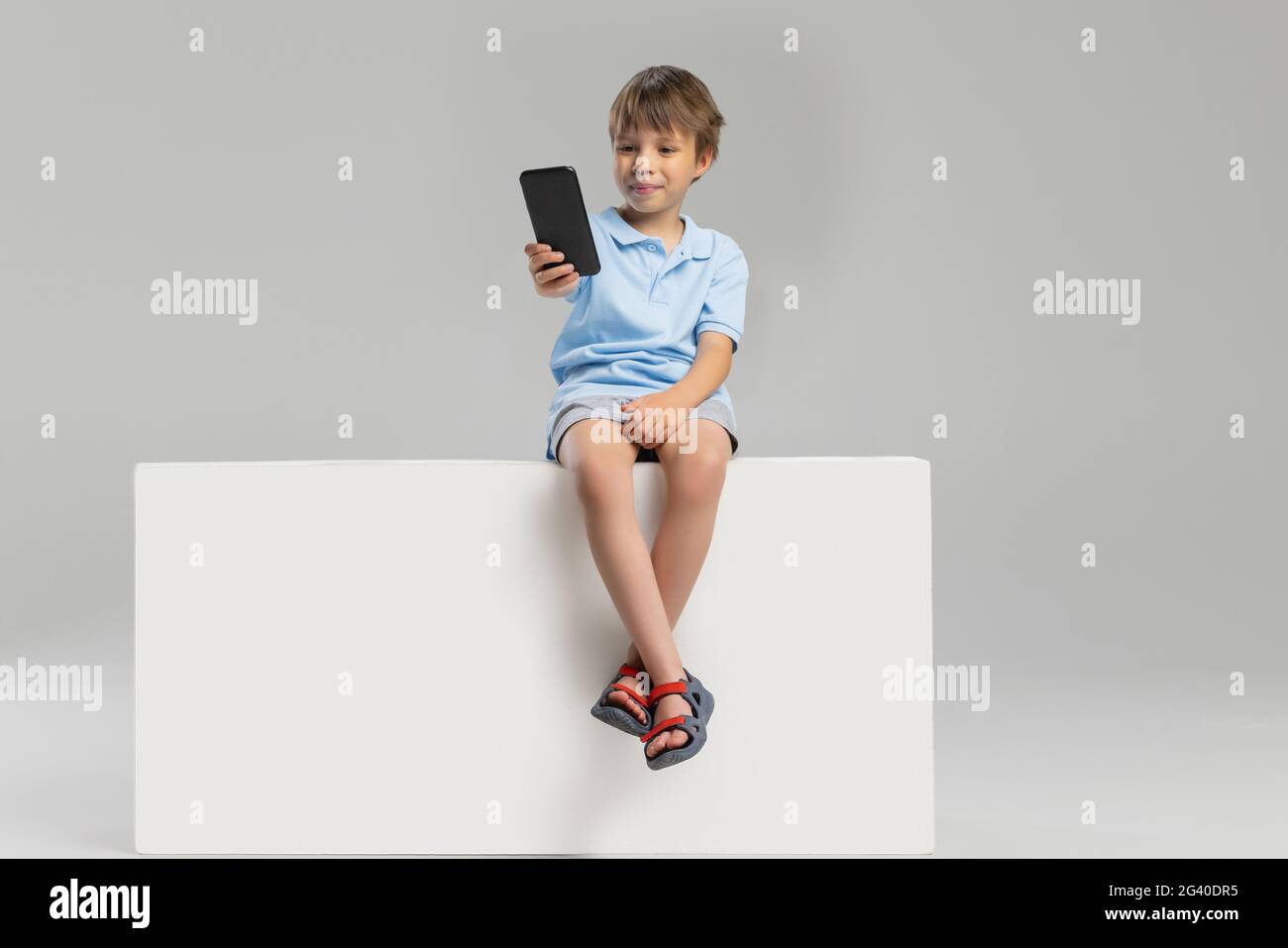 One Caucasian little boy in casual clothes sitting on box isolated over ...