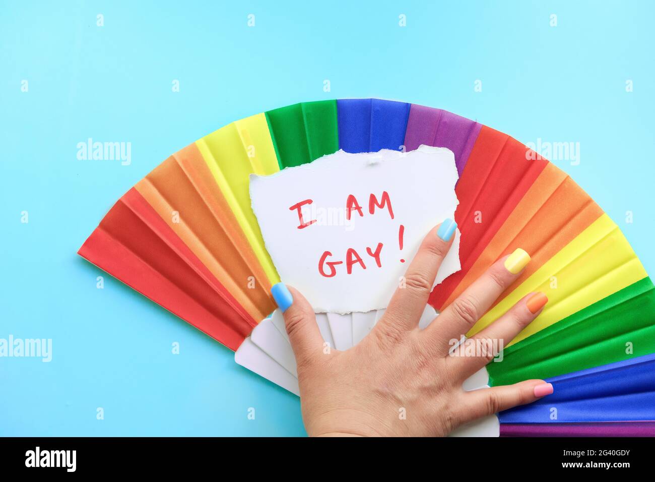 Text I am Gay on paper in hand with fake nails. Rainbow fan in colors ...