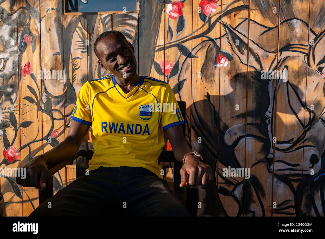 Young man with Rwanda jersey sits in front of mural with safari animal ...