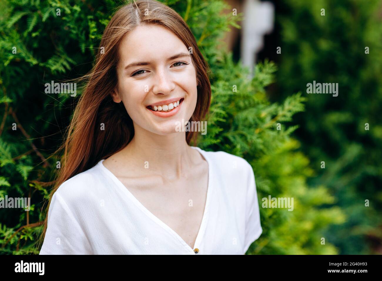 Beautiful, sincere, smiling girl posing on a background of green tree ...