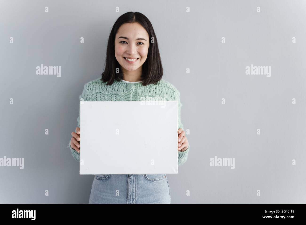 Young pretty woman smiles and holds blank piece of paper in her hands ...