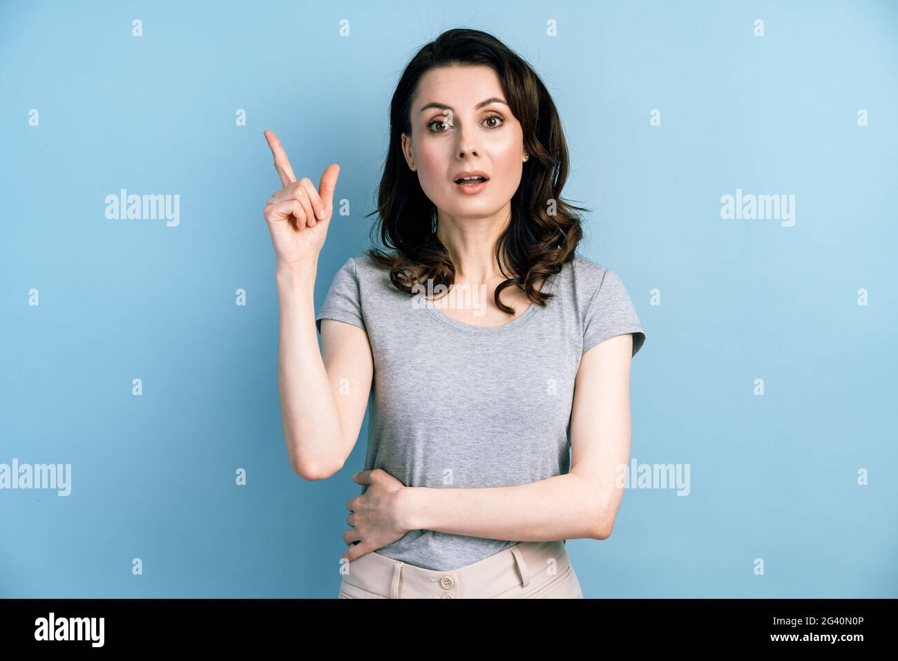 Pretty girl on a background of a blue wall, raised a finger up ...