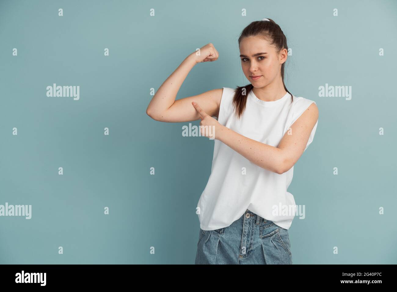 Close-up portrait of a nice girl showing arm muscles isolated on blue ...
