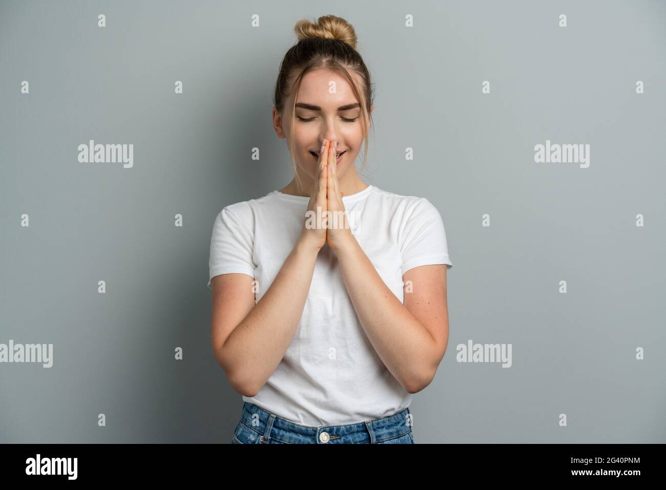 A young woman in a casual white T-shirt prays, clasping her hands ...