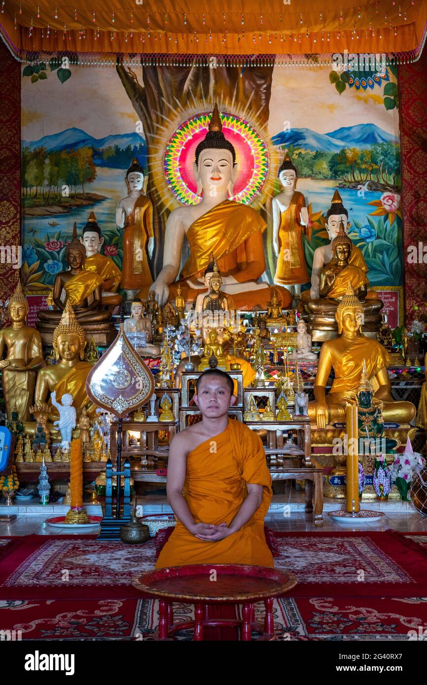 Young monk poses in front of Buddha statue at Vat Chom Khao Manilat Temple, Houayxay (Huay Xai ...