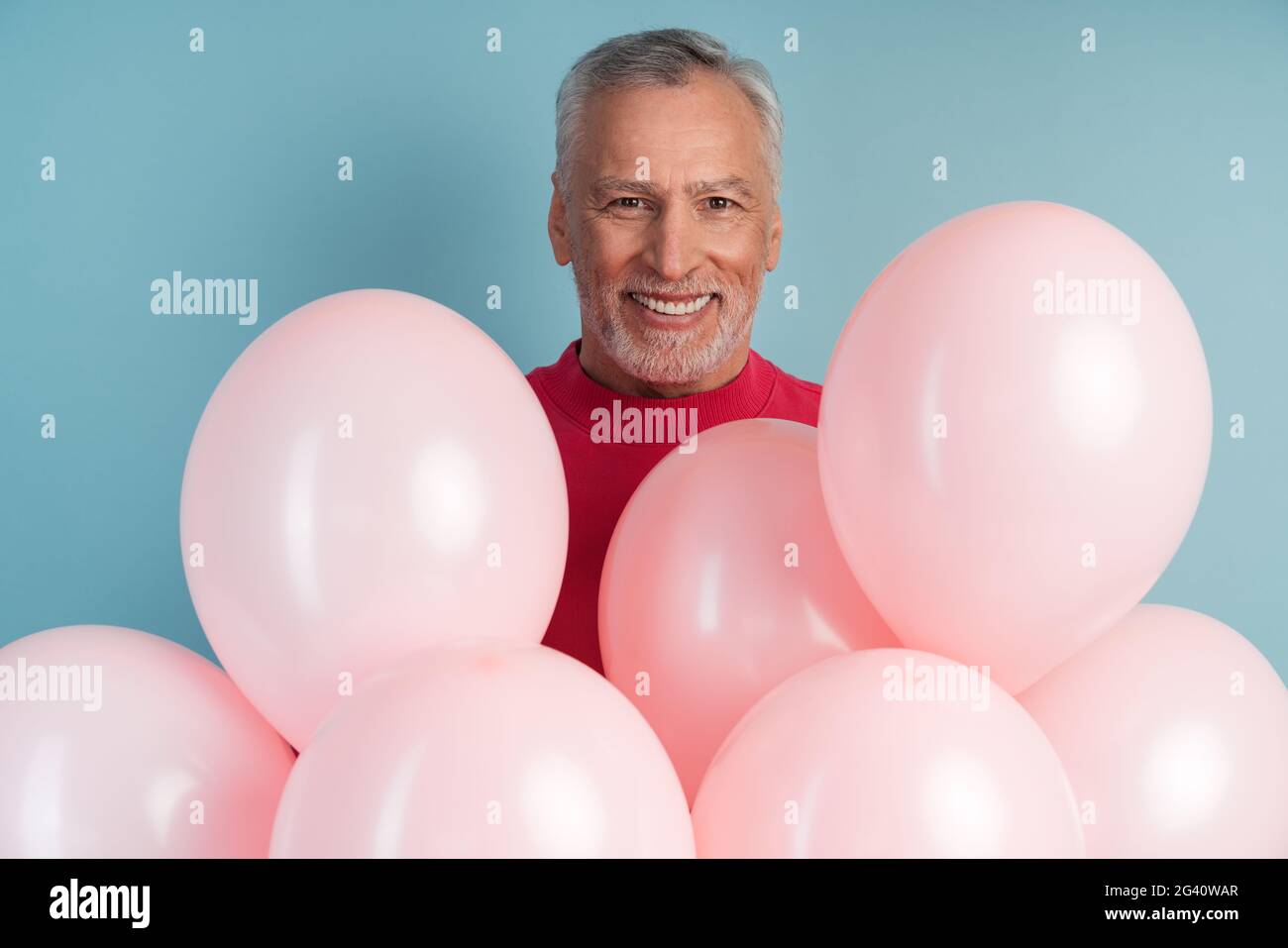 Positive, cheerful man with balloons posing on blue wall background ...