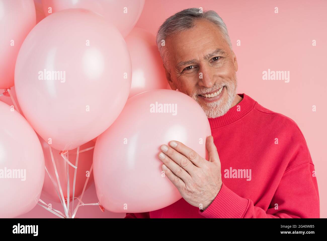 Positive, cheerful man with balloons posing on pink wall background ...