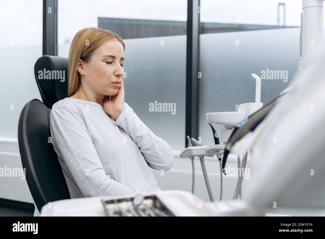 Pretty, young woman touches her cheek with her hand, wincing at the ...