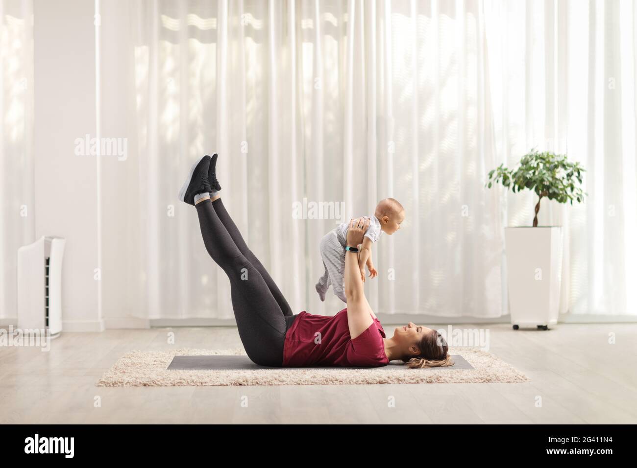Young mother exercising abs and holding a baby on the floor at home ...