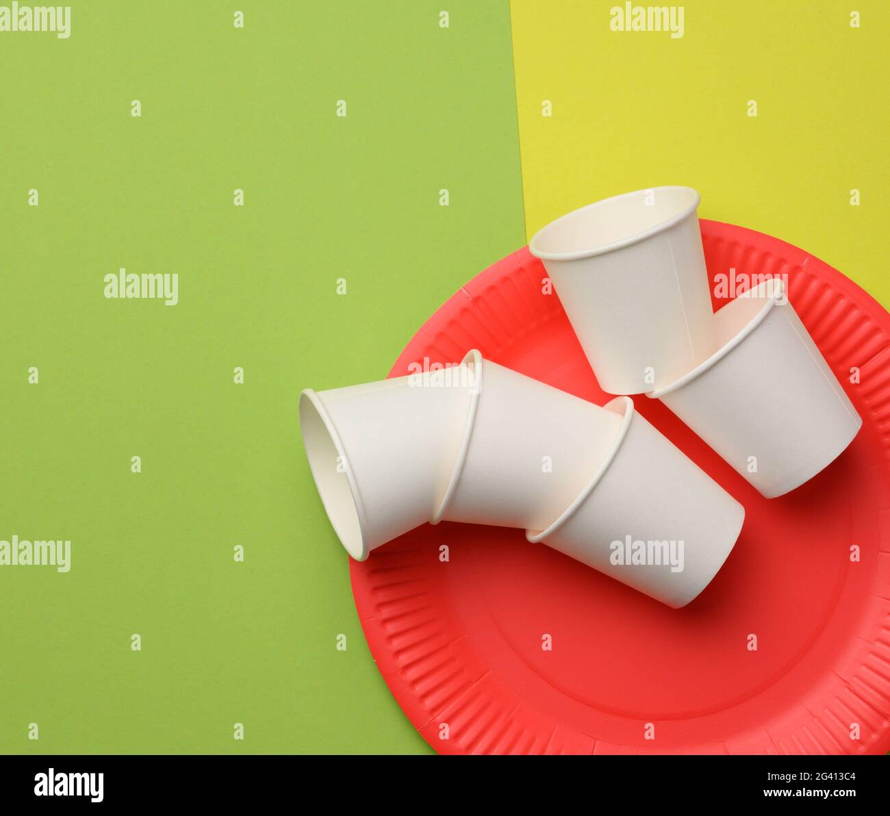 Stack of white paper cups and red round plates on a green background ...