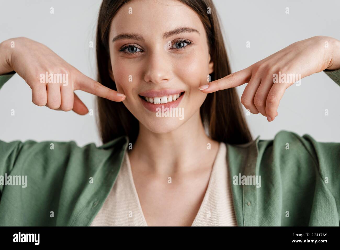 Happy caucasian girl smiling and pointing fingers at her cheeks ...