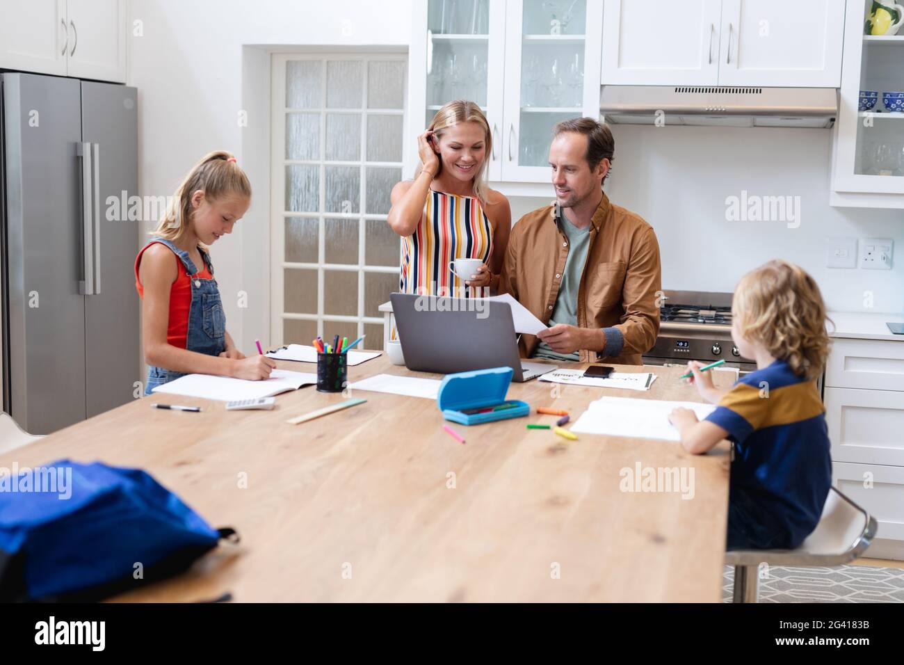 Caucasian father working at home on laptop talking to wife, with son ...