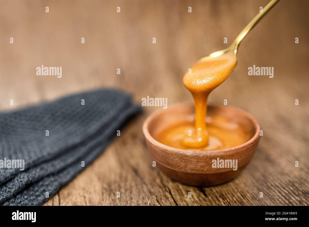Manuka honey from New Zealand dripping from golden spoon in wooden bowl ...