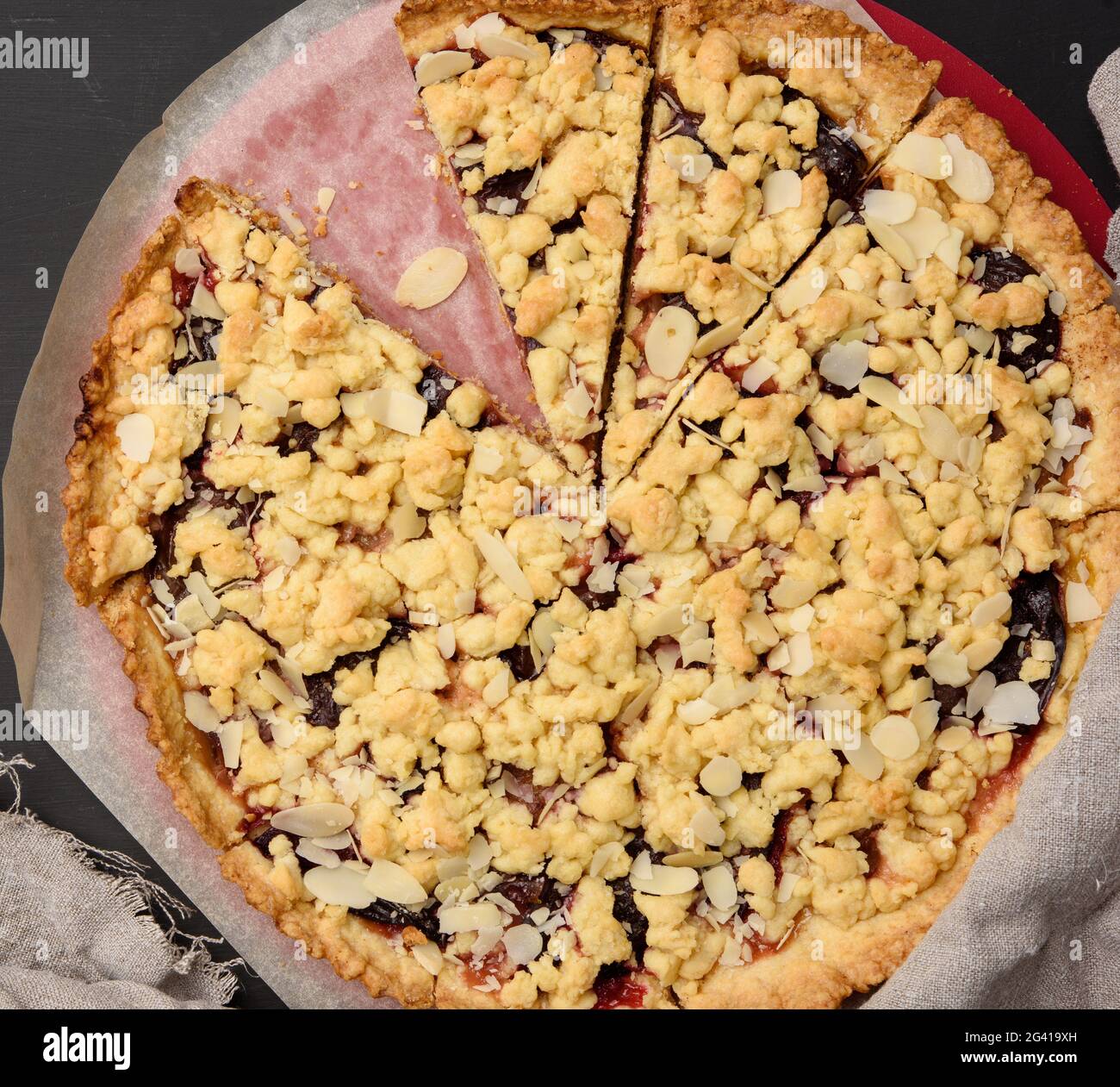 Baked round crumble pie with plum cut into pieces on a black background ...