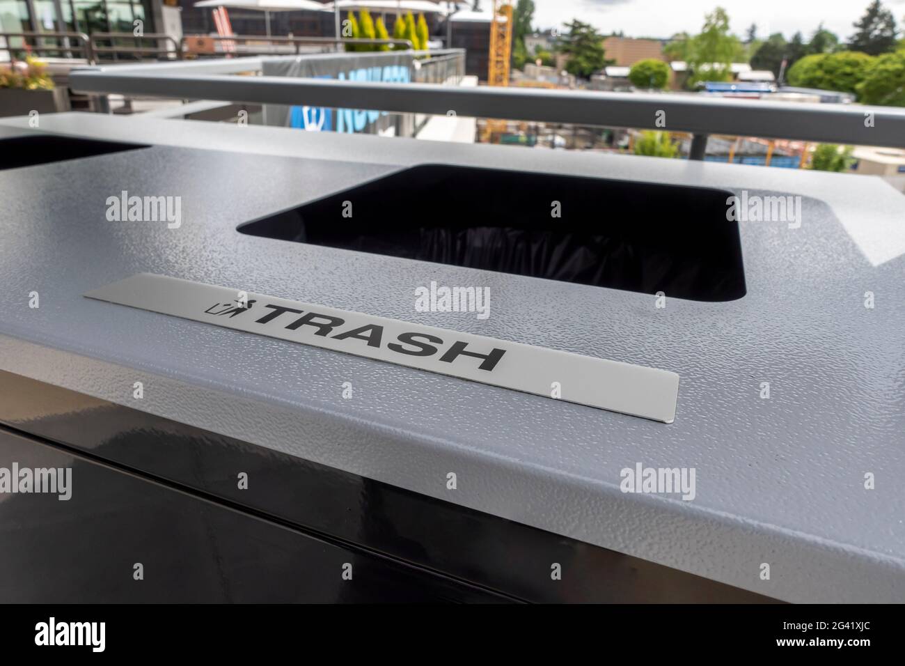 Angled view of a covered, grey and black outdoor trash bin labelled for ...