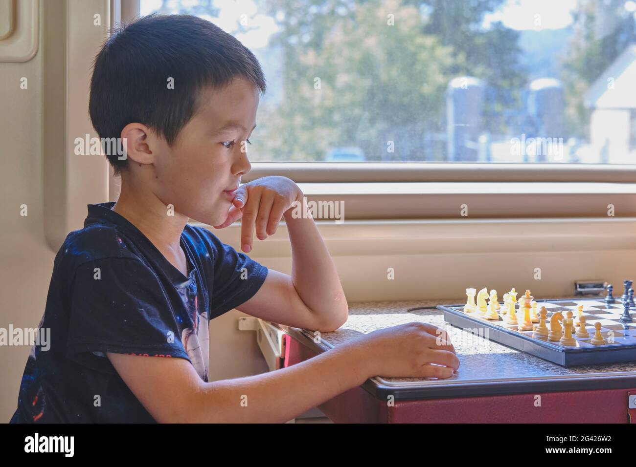Young boy playing chess near window in the train. Table games concept ...