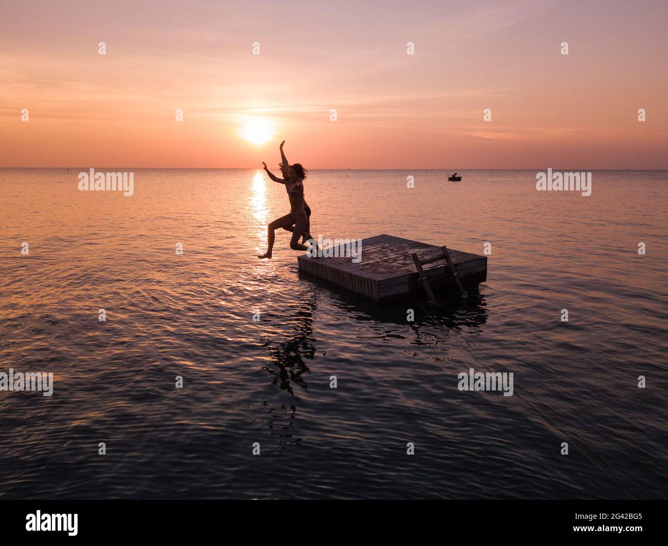 Aerial view silhouette of young couple jumping from a bathing platform ...