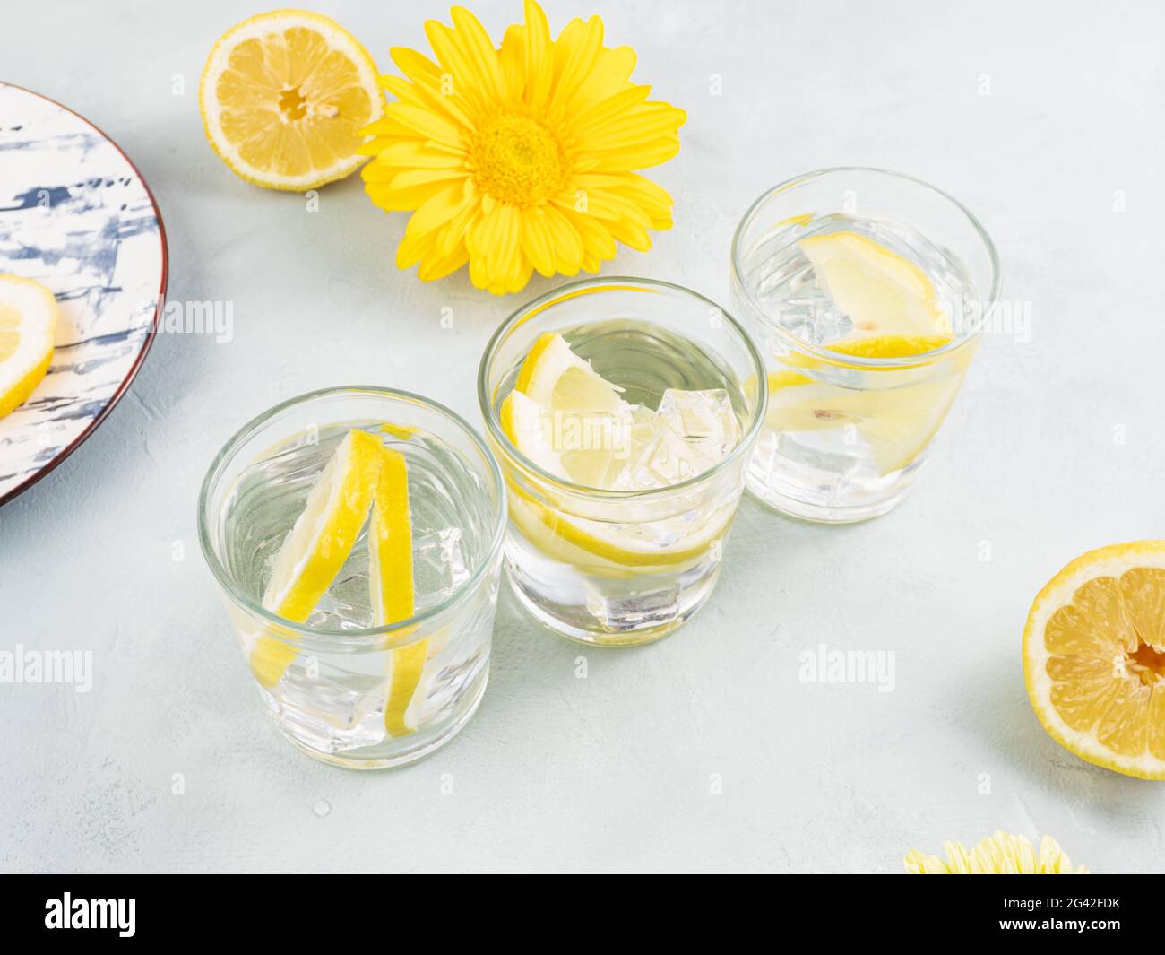 Lemon water drink with ice cubes on stone background with gerbera daisy ...