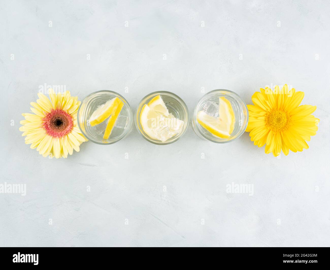 Lemon water drink with ice cubes on stone background with gerbera daisy ...