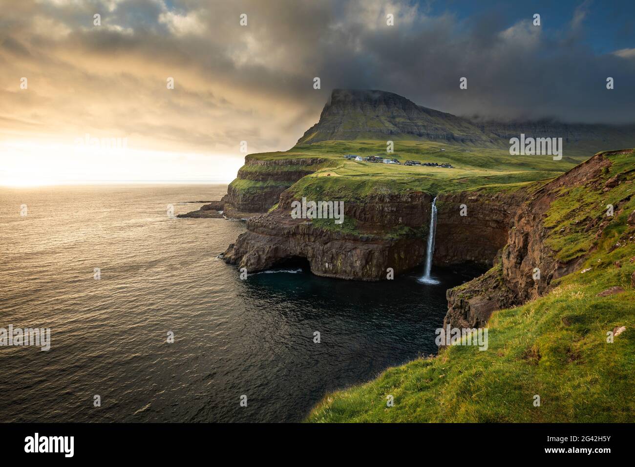Sunset At The Múlafossur Waterfall With The Village Of Gásadalur On The