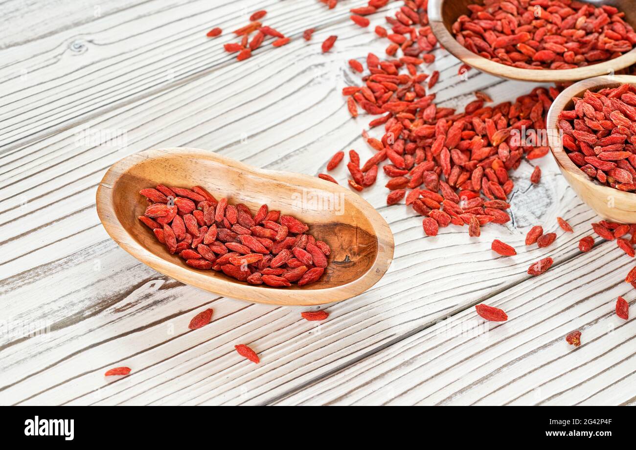 Dried goji aka. wolfberry seeds in wooden bowls and spilled on white ...