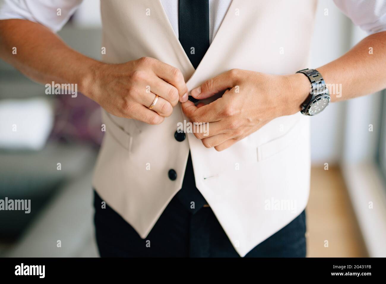 A man buttoning the vest of his suit in a hotel room while preparing ...