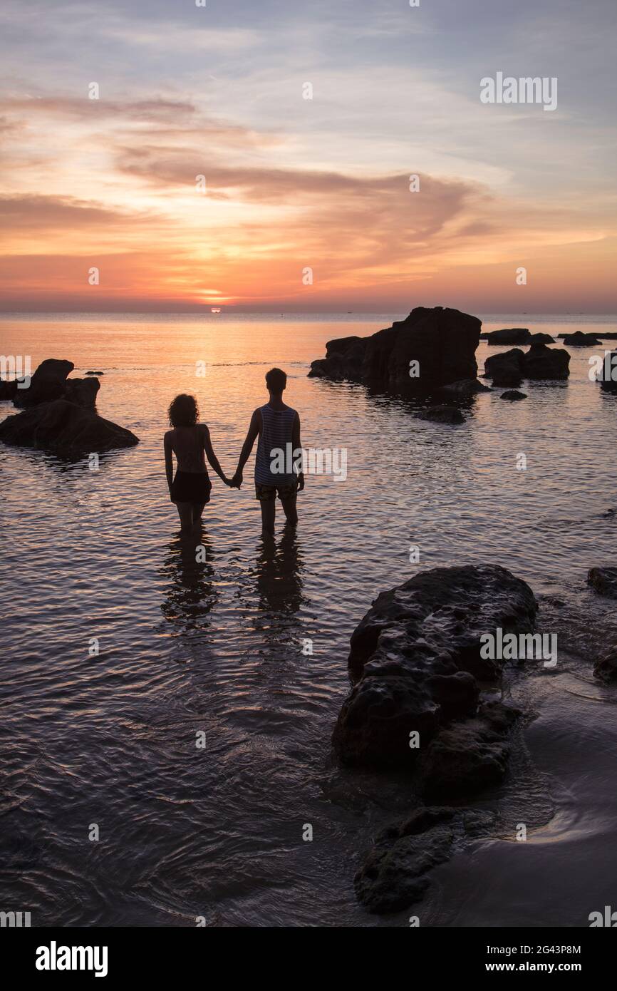 Silhouette of young couple holding hands on Ong Lang Beach at sunset ...
